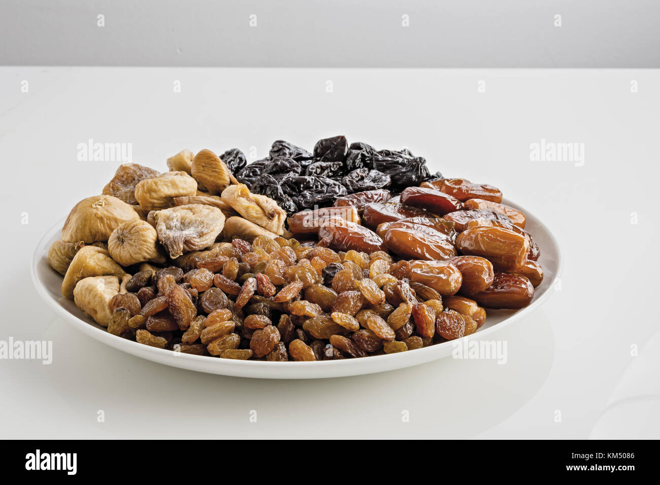 dates plums figs raisins round plate 4 white background Stock Photo - Alamy