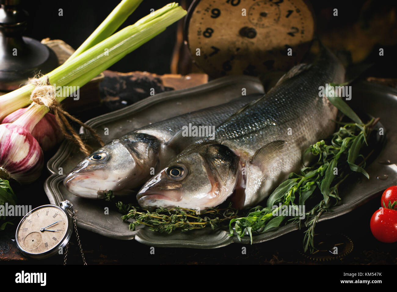 Still life with raw fish seabass, herbs, vegetables and vintage clock ...
