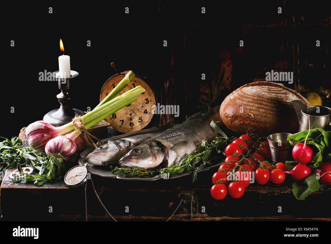 Still life with raw fish seabass, herbs, vegetables and vintage clock ...