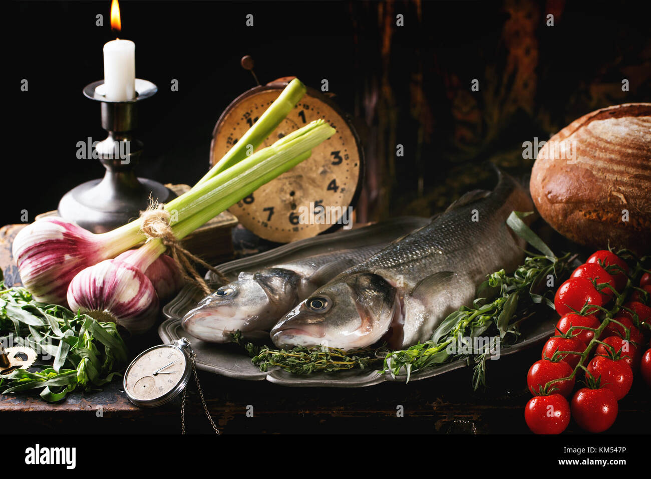 Still life with raw fish seabass, herbs, vegetables and vintage clock ...