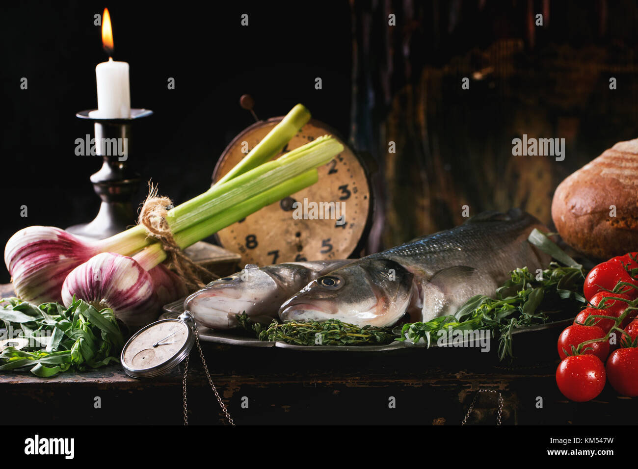 Still life with raw fish seabass, herbs, vegetables and vintage clock ...
