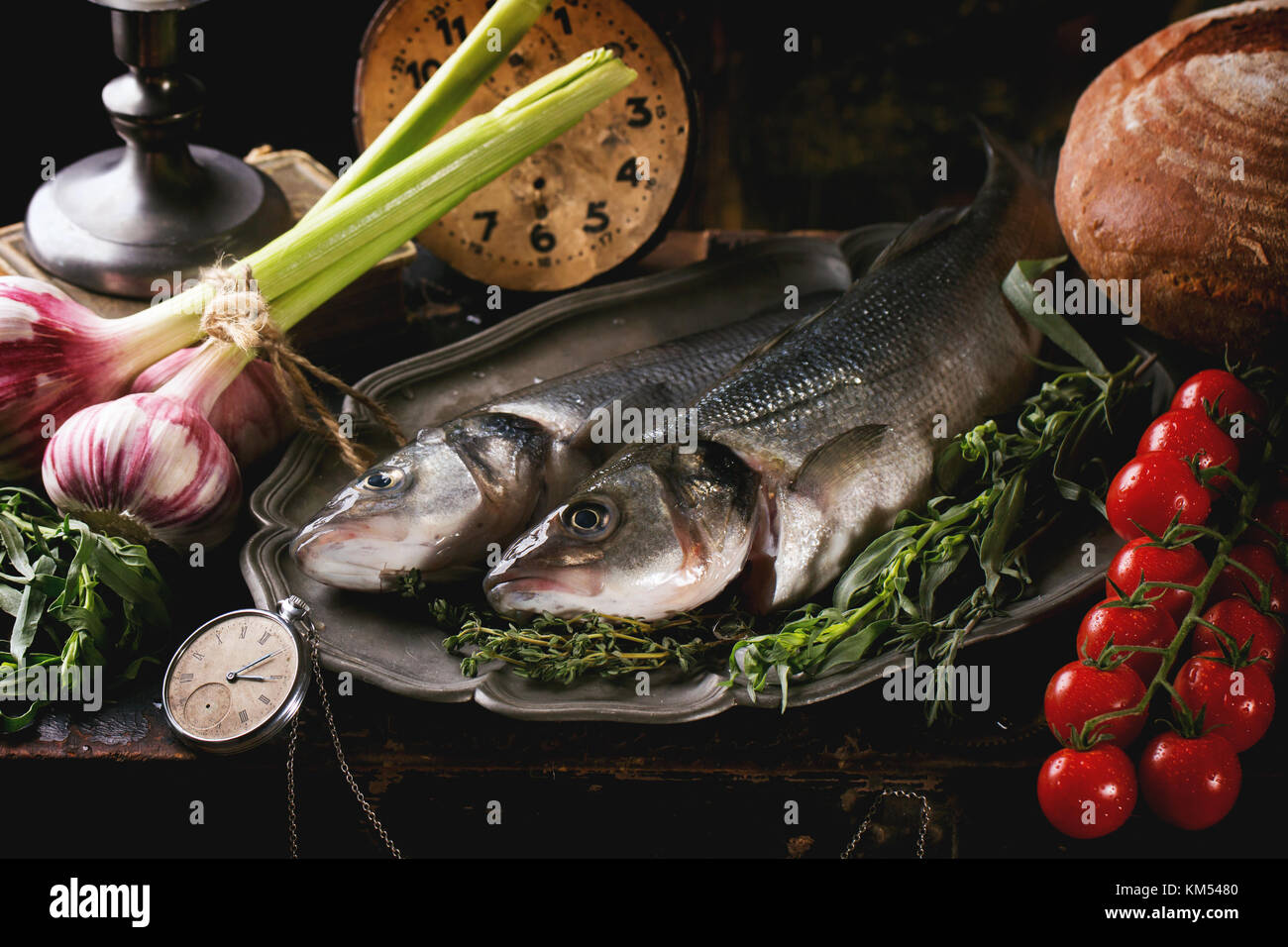 Still life with raw fish seabass, herbs, vegetables and vintage clock ...