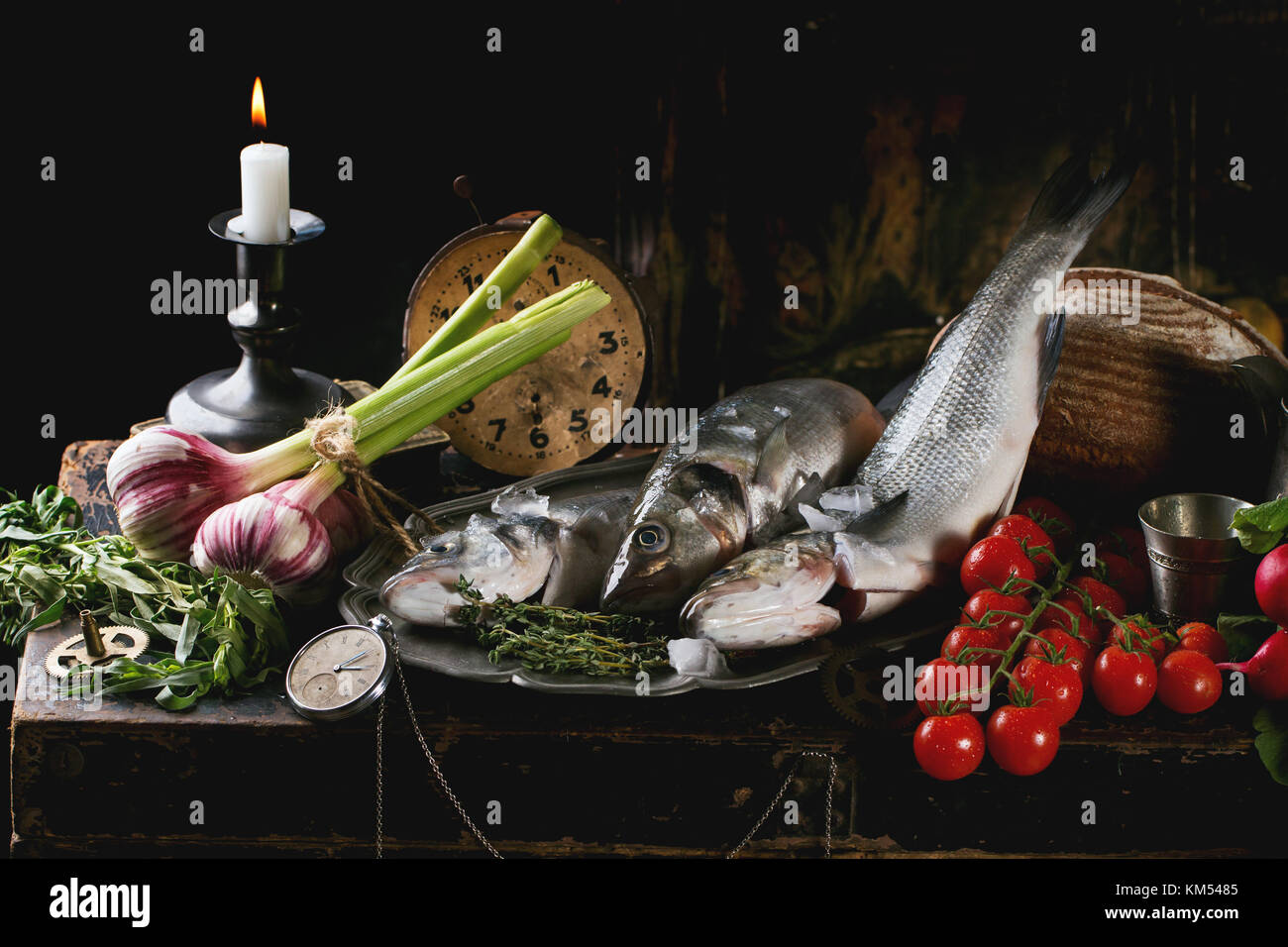 Still life with raw fish seabass, herbs, vegetables and vintage clock ...