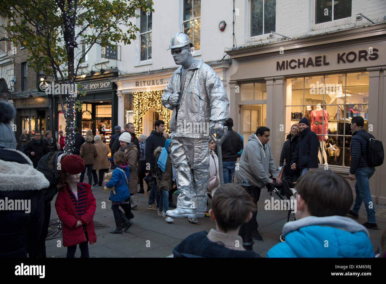 Silver painted living statue street performer sits totally still as if ...