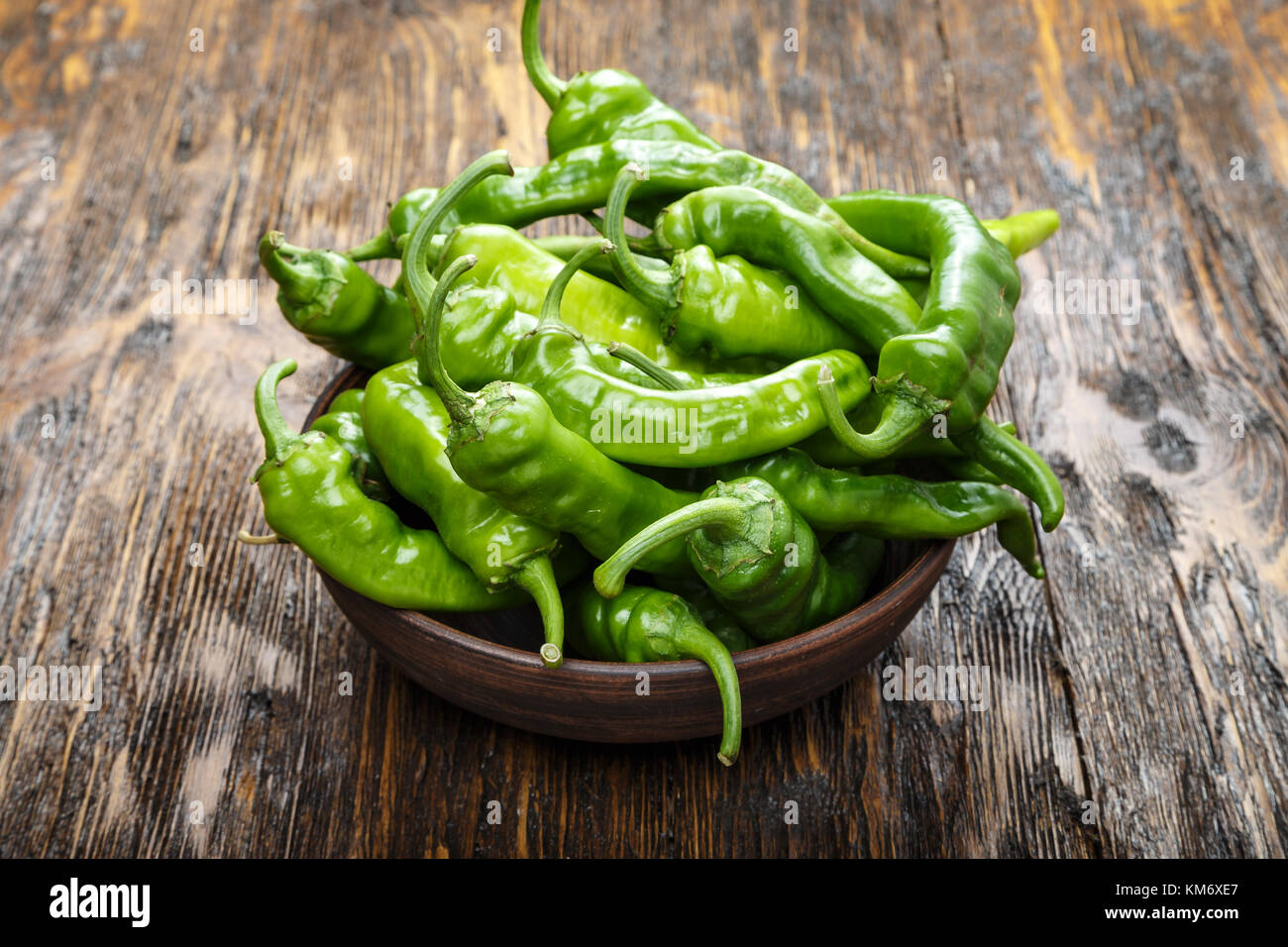 green chili peppers placed in a clay plate on a brown wooden table ...