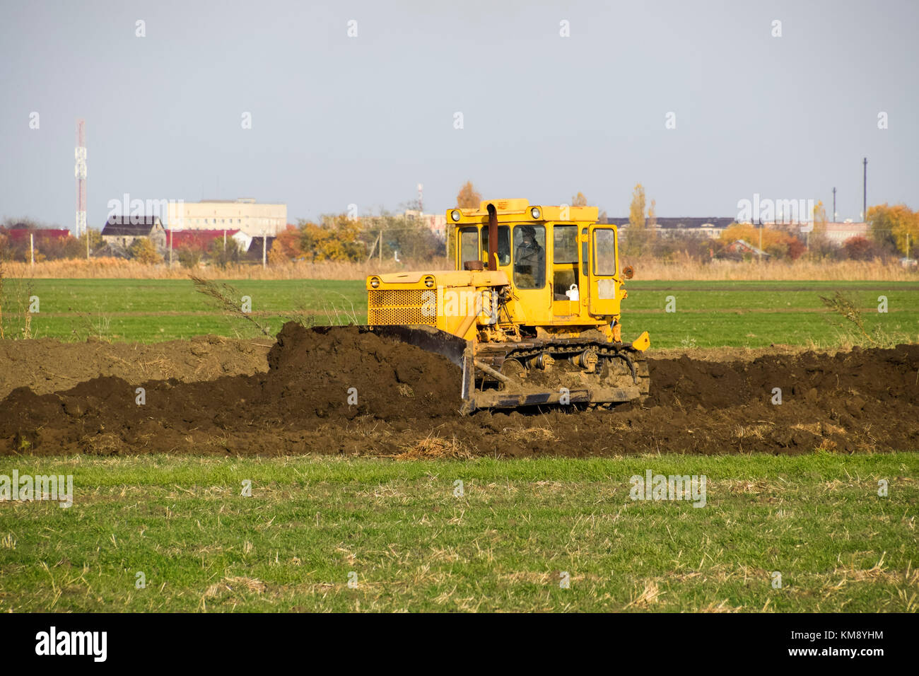 The yellow tractor with attached grederom makes ground leveling. Work ...