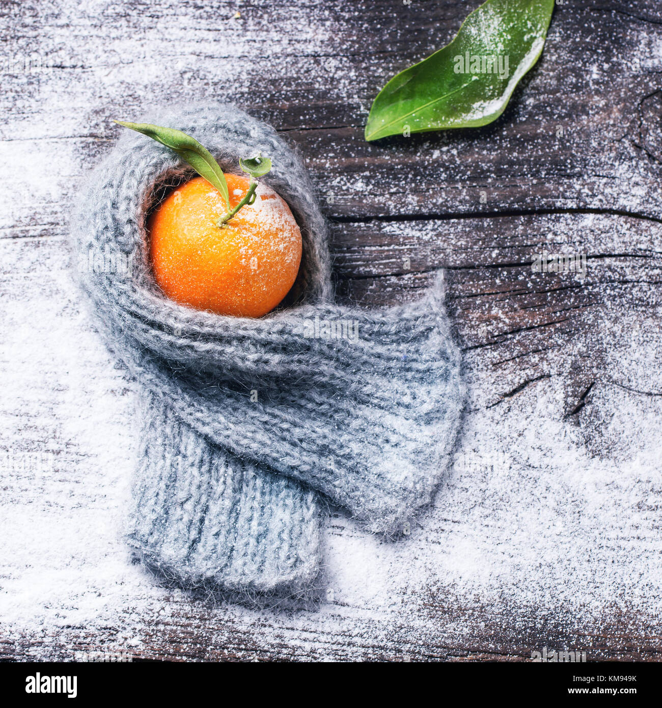 Tangerine in scarf over wooden background with snow and leaf. Top view ...