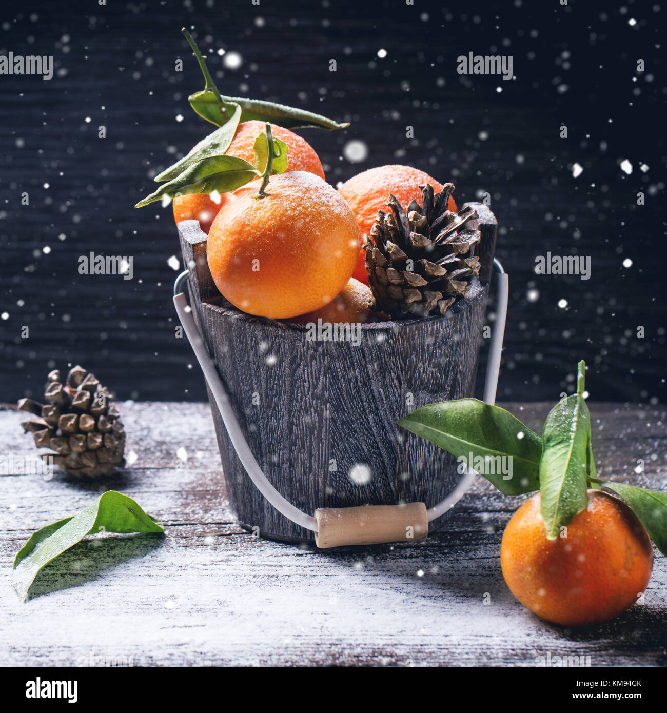 Wooden bucket with tangerines over wooden background with snow and cone ...