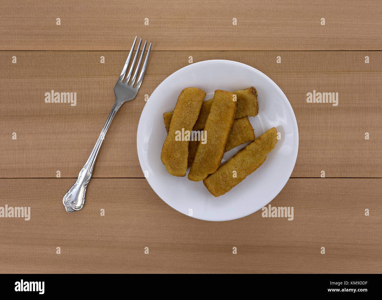 Top view of a serving of French toast sticks on a plate with a fork to ...