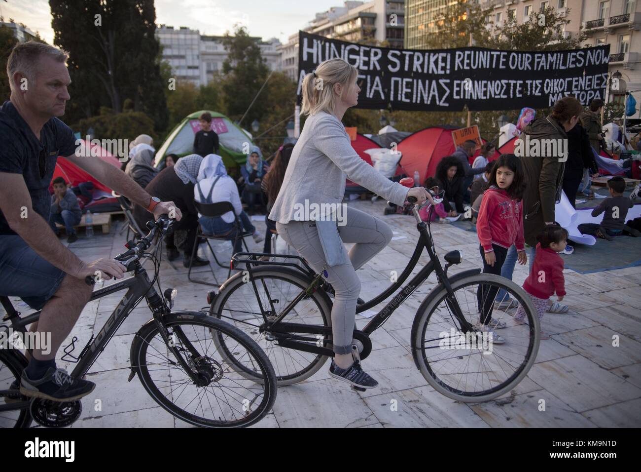Tourists in Athens passing by bicycle Refugee tents. Refugees on hunger ...
