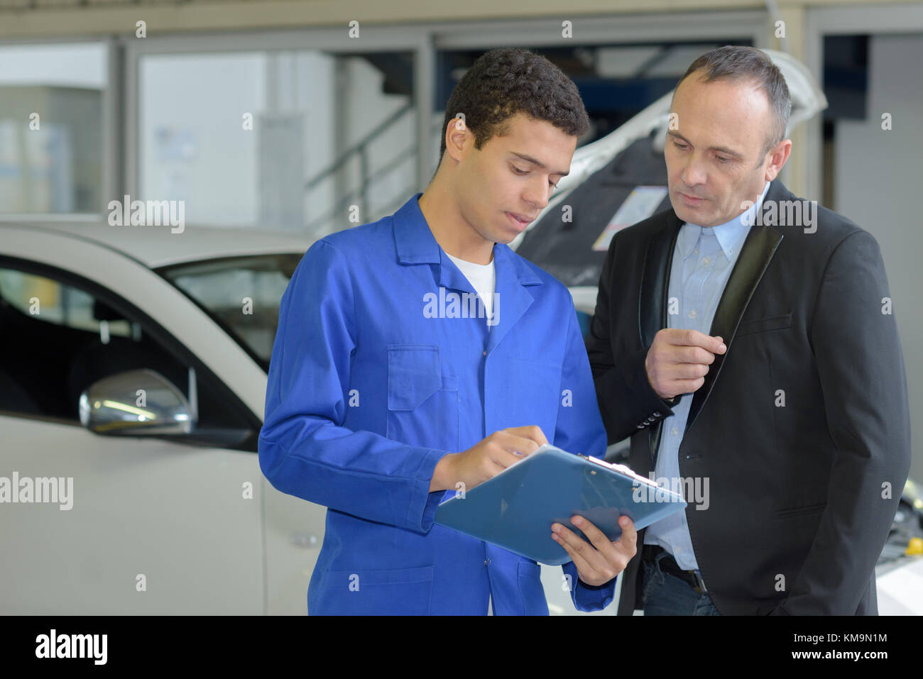 young mechanic showing bill to mature man client Stock Photo - Alamy