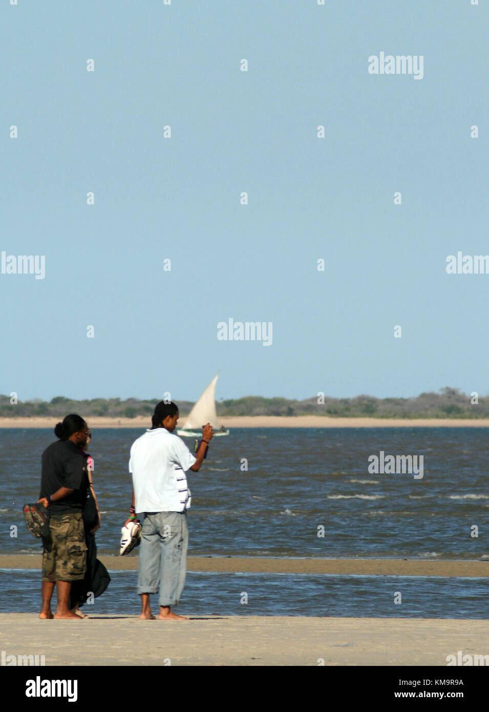 Maputo, Mozambique, people standing on the beach with a sailboat in the ...