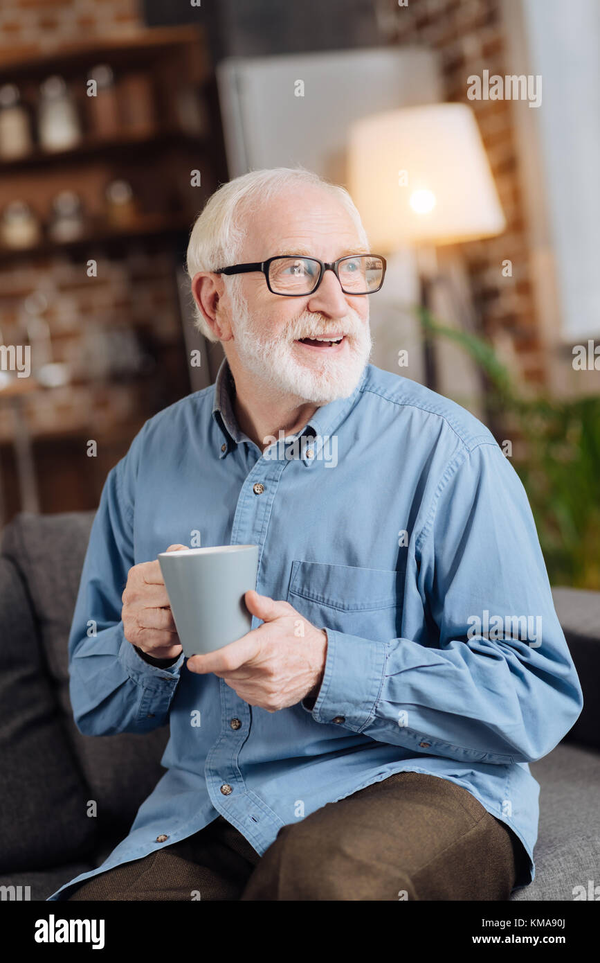 Cheerful man drinking tea while sitting on sofa Stock Photo - Alamy