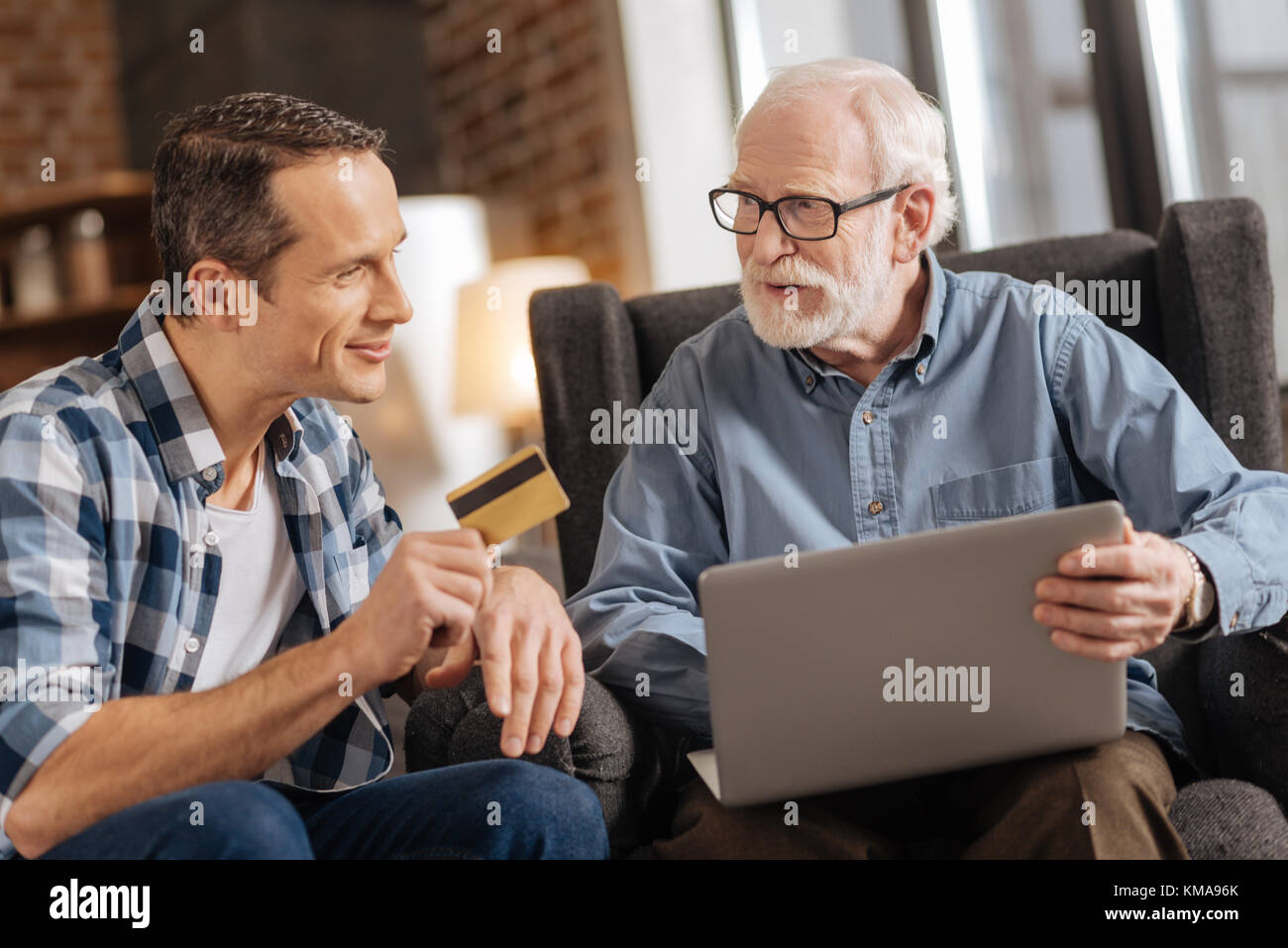 Young man giving bank card to his father using laptop Stock Photo - Alamy
