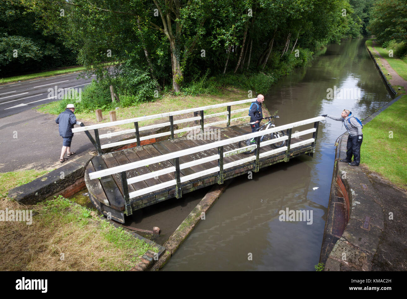 A cyclist stands on a swing bridge whilst two others move the bridge ...