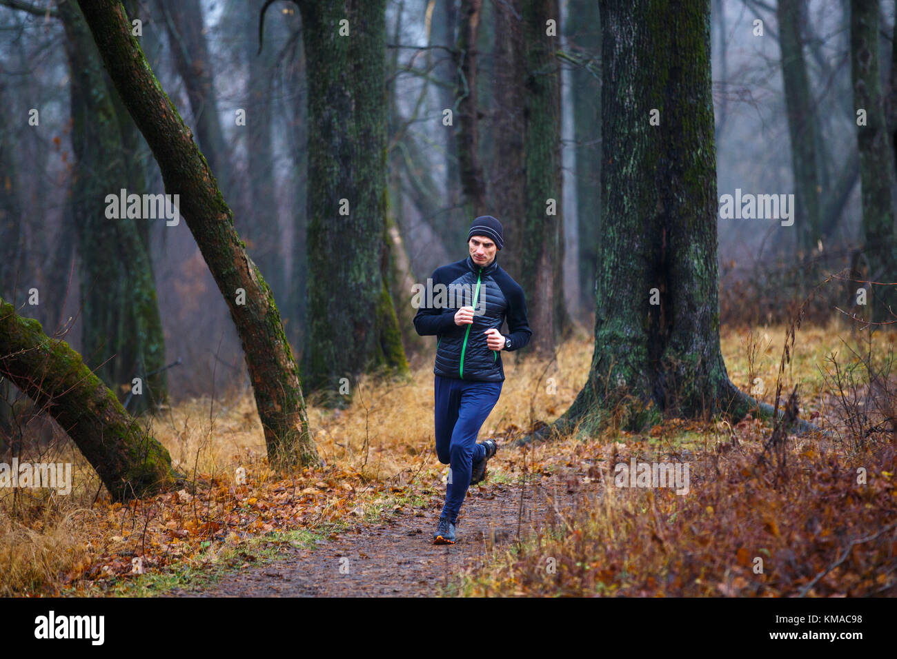 Young man jogging in fall park. Trail running in cold and misty weather ...