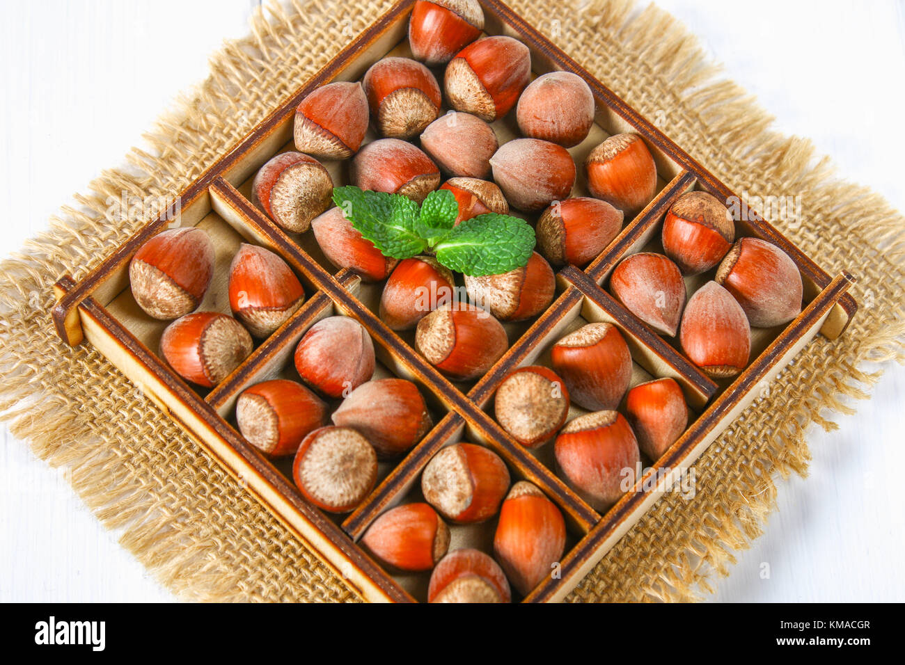 Walnut hazelnuts in a square wooden box with dividers on a white wooden ...