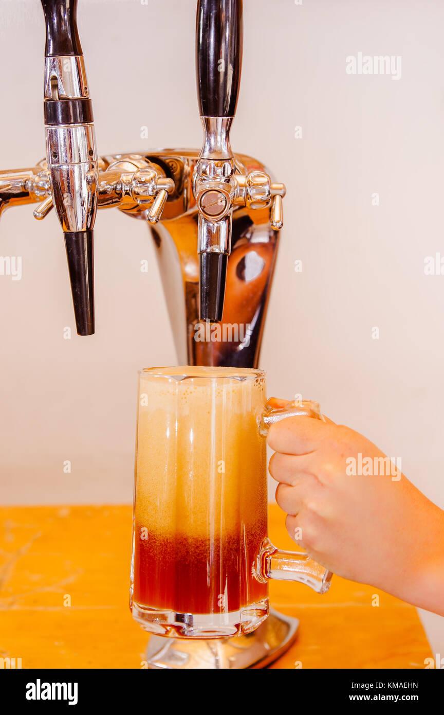 Barman hand at beer tap pouring a draught lager beer serving in a ...