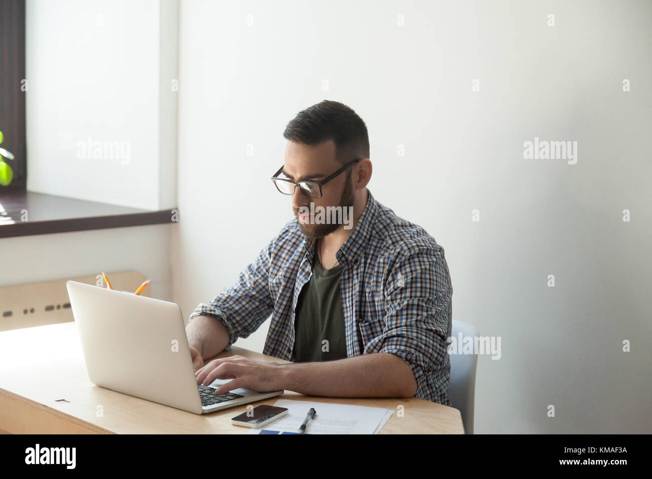 Millennial businessman sitting and typing on laptop in home office ...