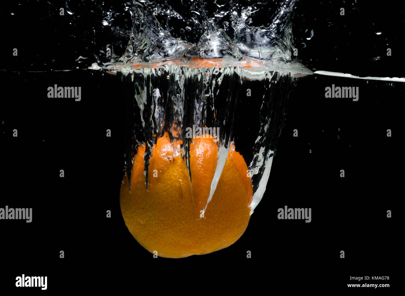 Single orange falling into splashing water, isolated on black ...