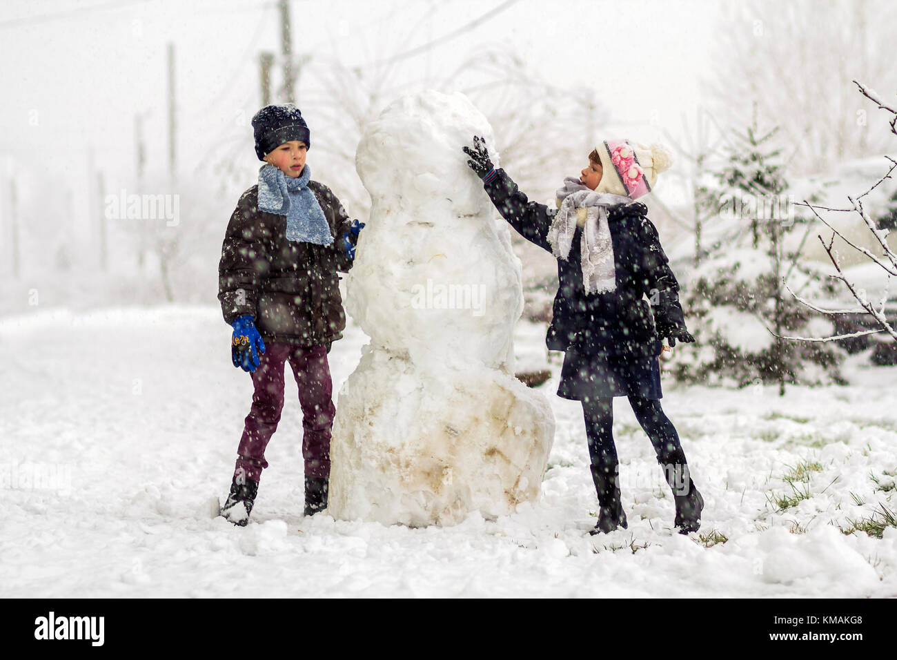 Children boy and girl outdoors in snowy winter are making a big snowman ...