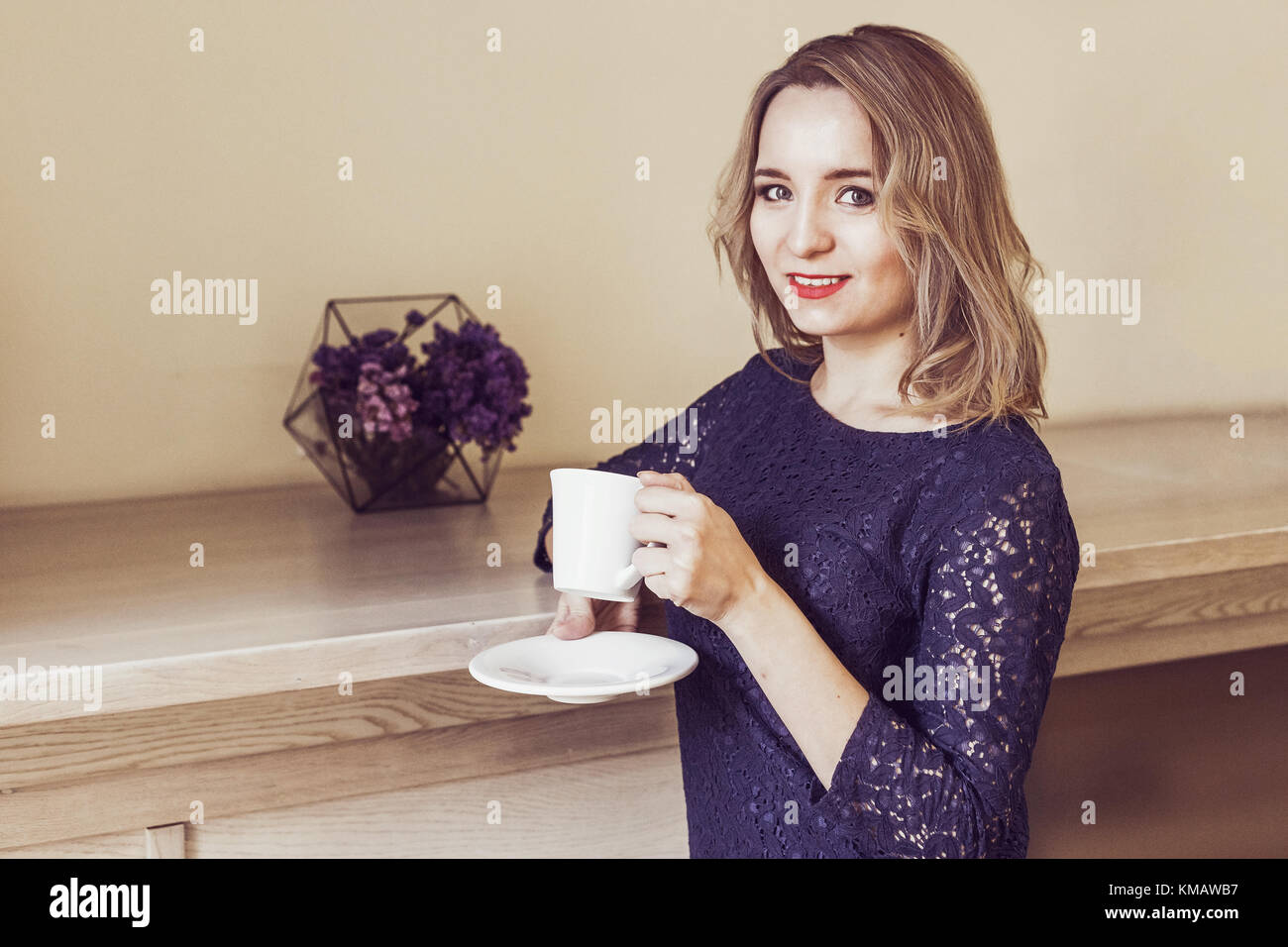 Beautiful young woman drinking tea or coffee standing by the high table ...