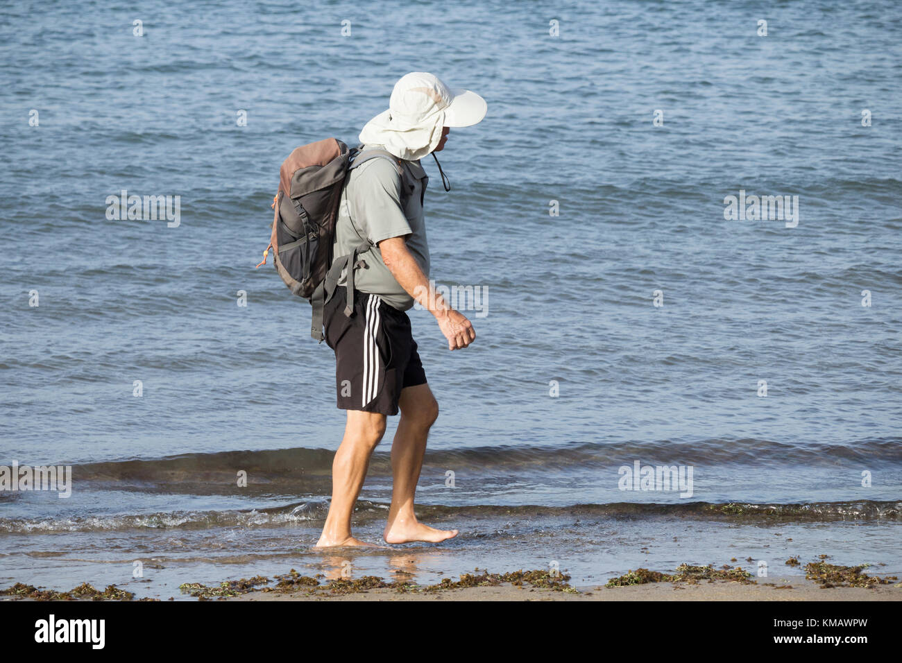 Man walking on beach wearing hat to protect from sun. Hat has a large ...