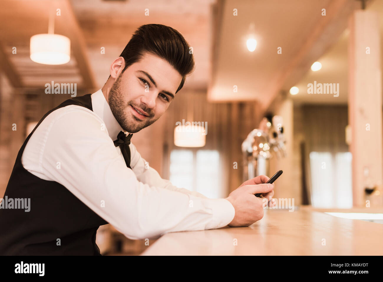 Waiter sitting at bar counter with smartphone Stock Photo - Alamy