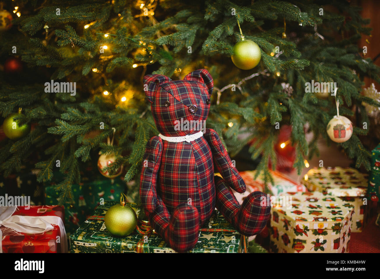 Teddy bear gift sitting under decorated with lights Christmas tree with ...