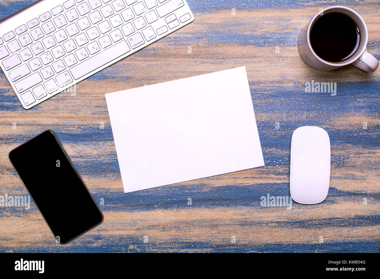 Office workplace with keyboard, empty paper, mobile phone, cup of tea ...