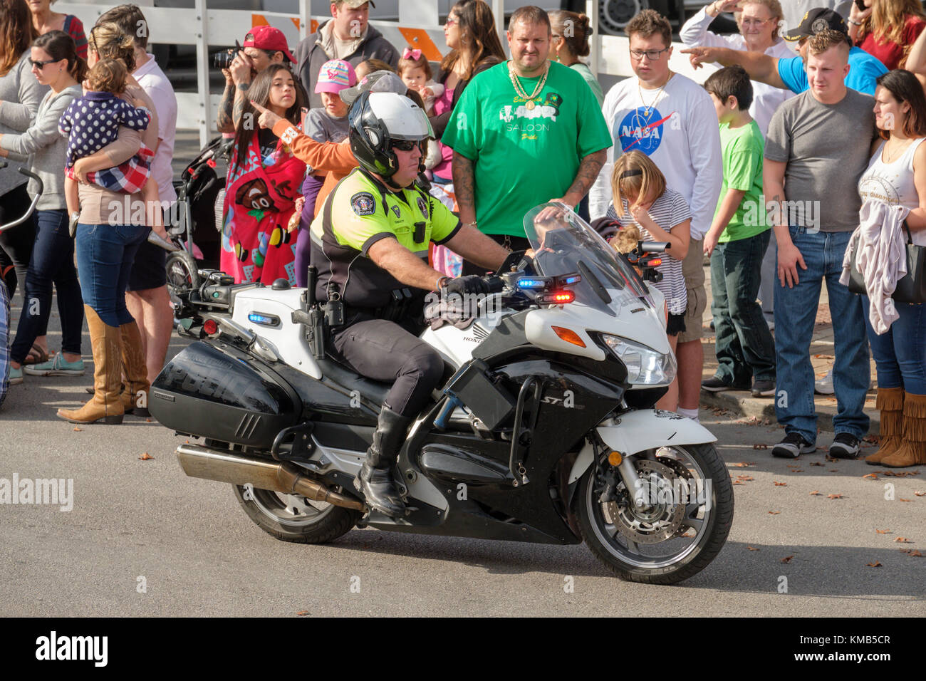 Policeman riding motorcycle on street next to crowd lining parade route ...