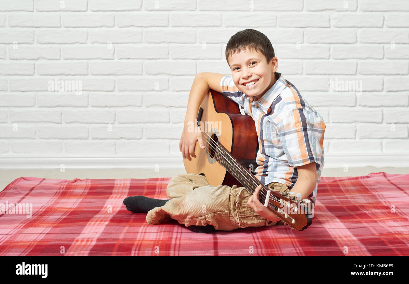 boy playing music on guitar, sitting on a red checkered blanket, white ...
