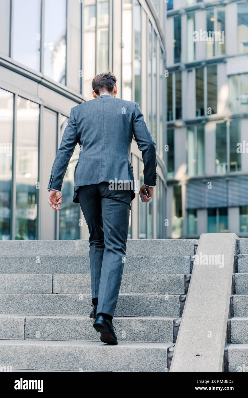 businessman walking upstairs in an office park with a smartphone in the ...
