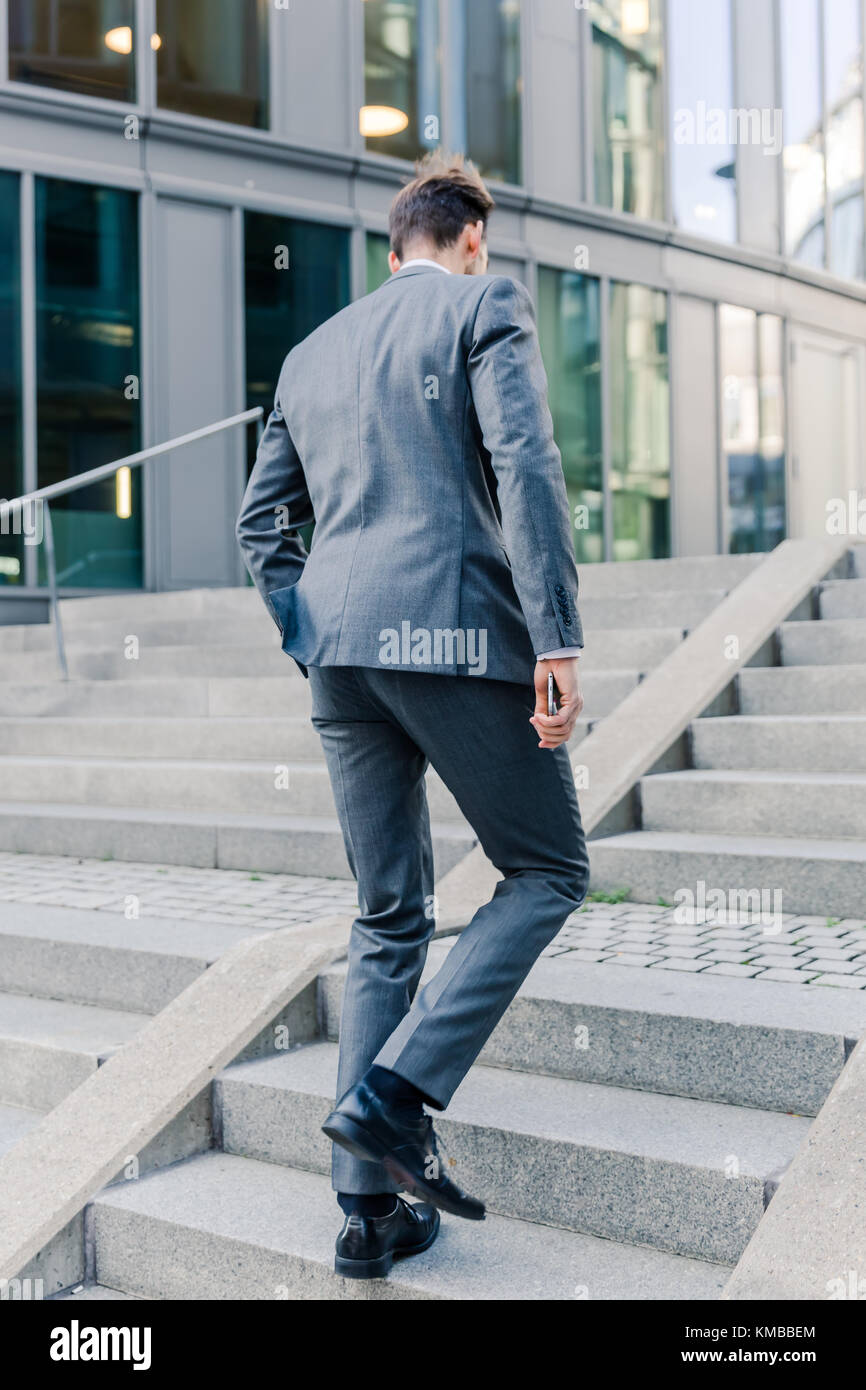 businessman walking upstairs in an office park with a smartphone in the ...