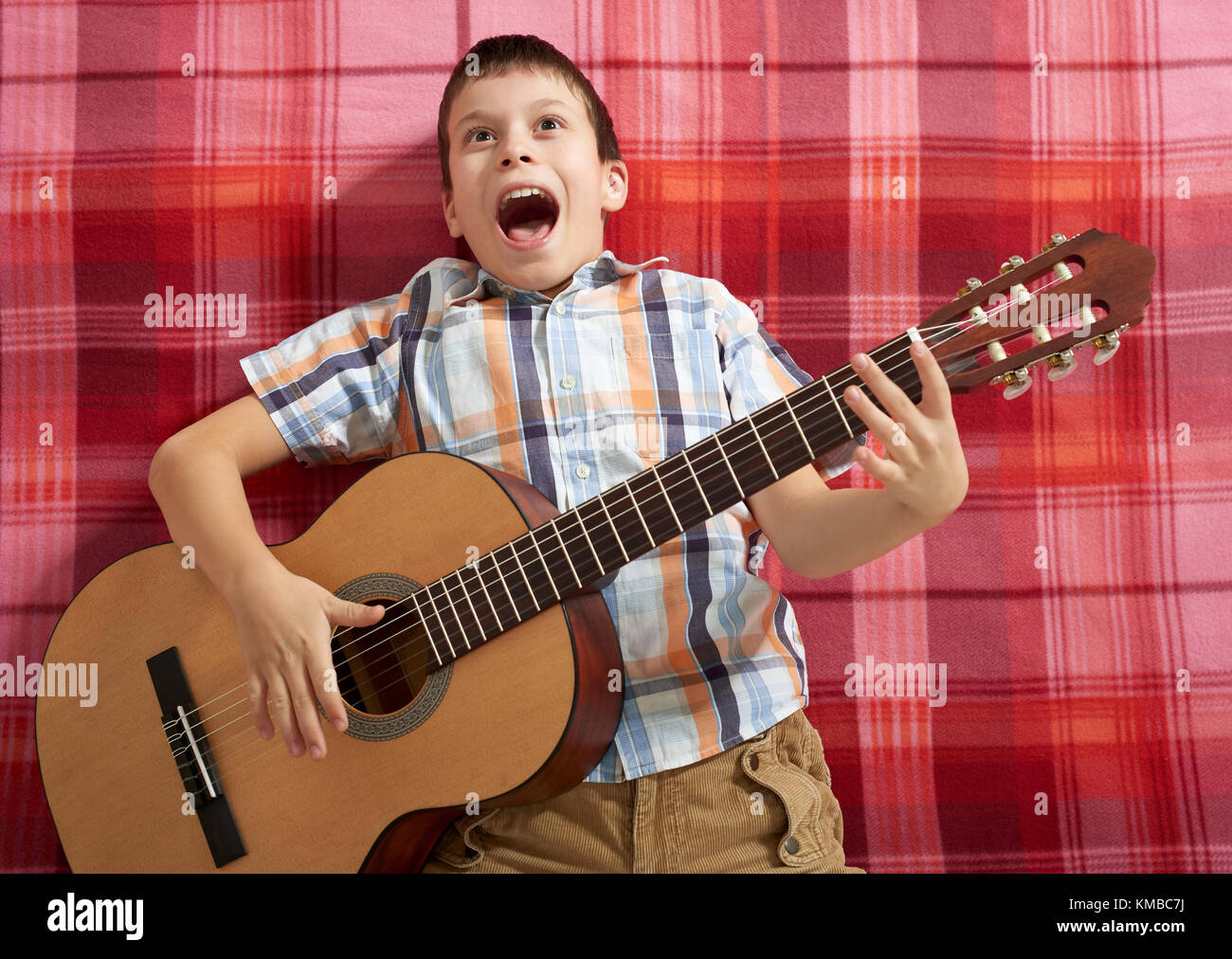 boy playing music on guitar, lies on a red checkered blanket, top view ...