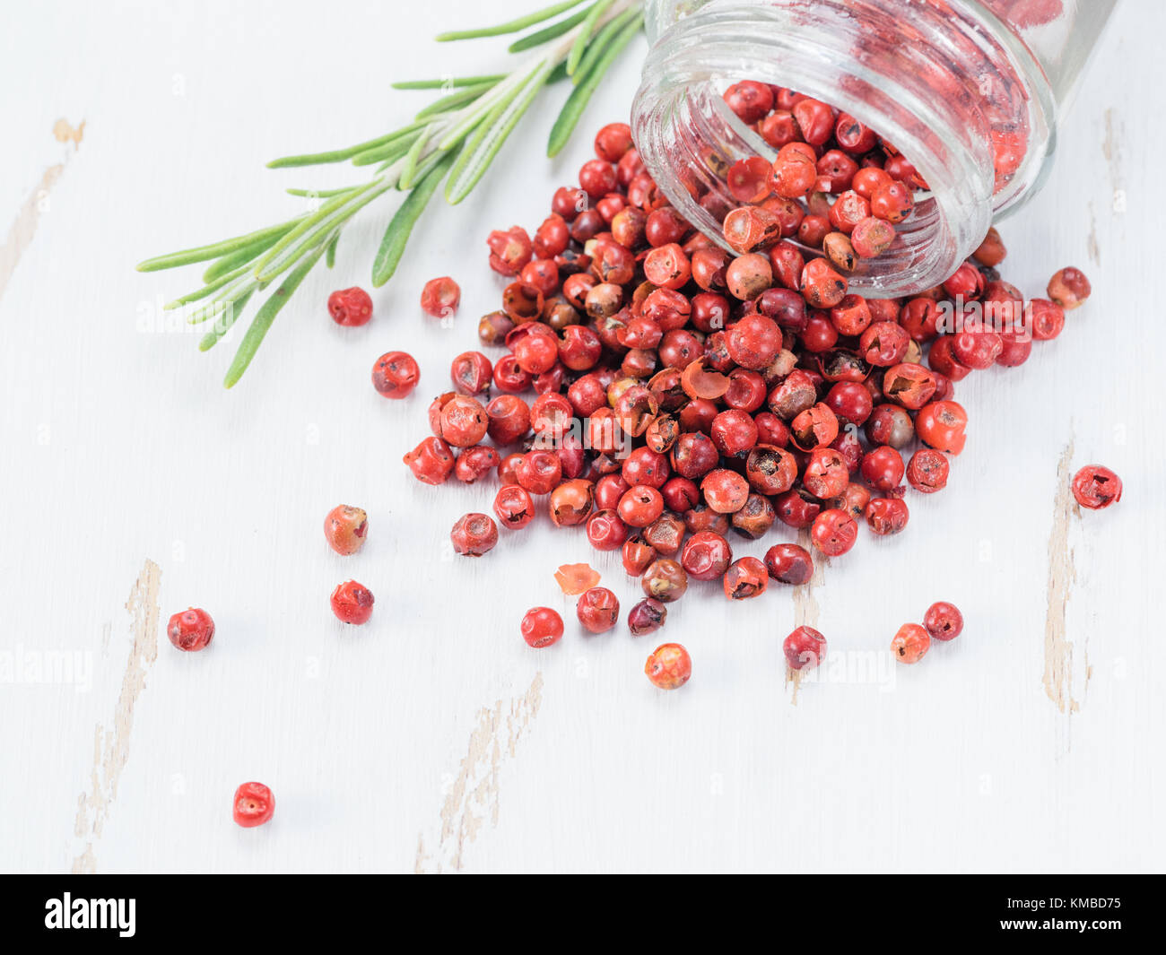 Dried pink pepper berries poured from glass jar on white wooden cutting ...