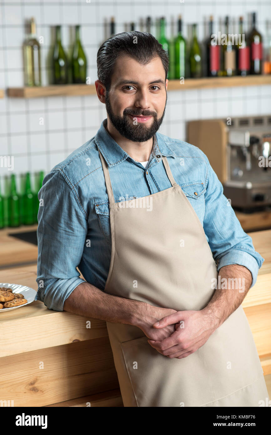 Calm friendly owner of a comfortable cafe standing and smiling kindly ...