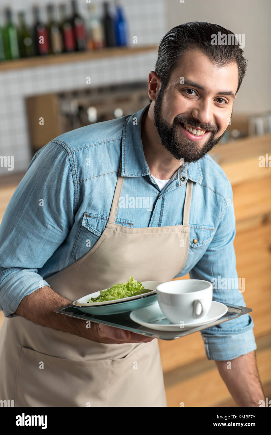Positive responsible waiter smiling while taking the dirty dishes Stock ...