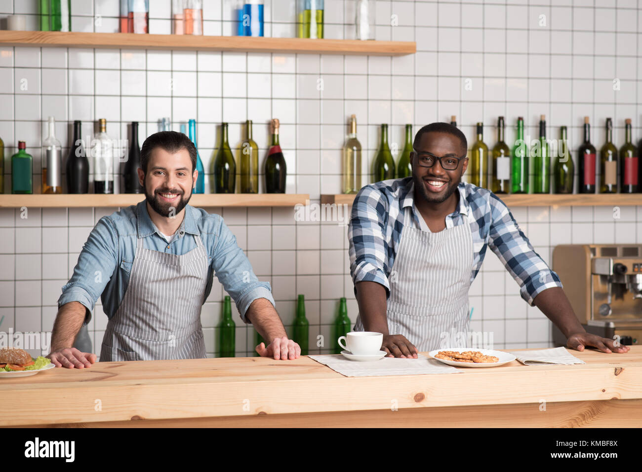 Two positive waiters standing at the bar counter and smiling cheerfully ...
