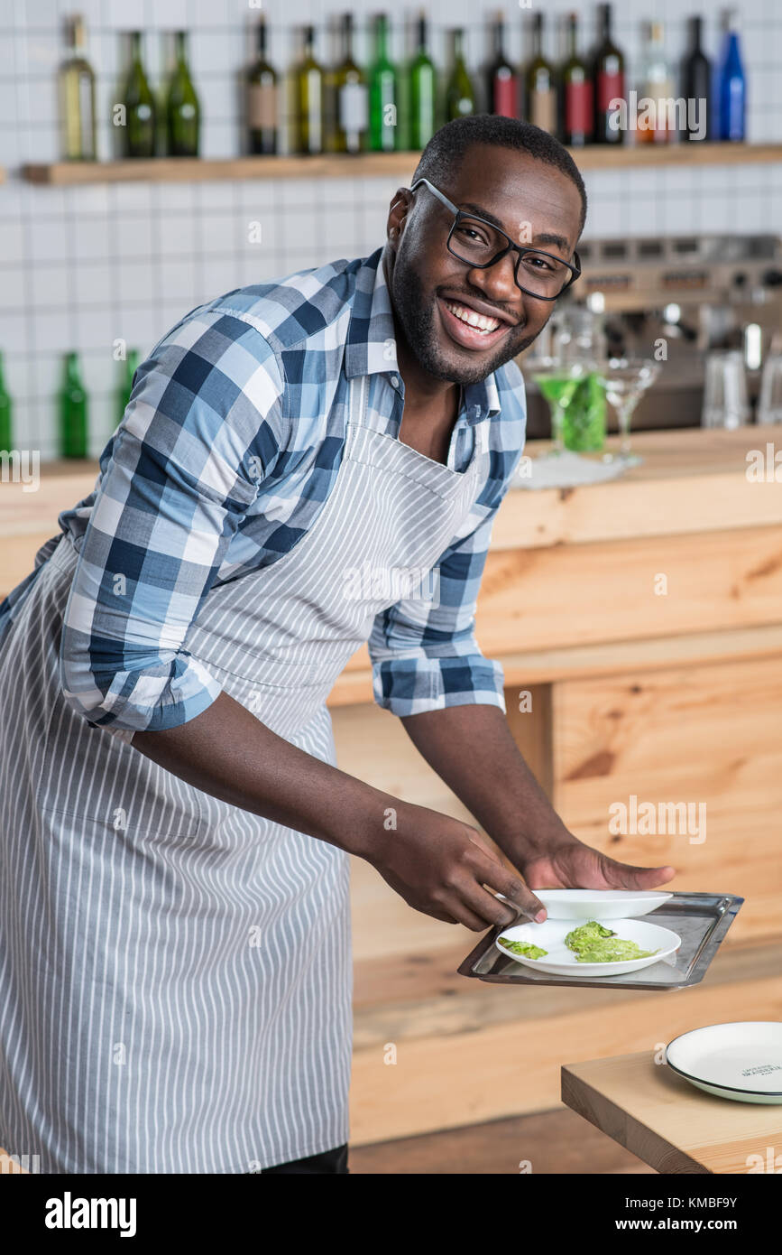 Handsome young waiter taking dirty dishes and looking positive Stock ...