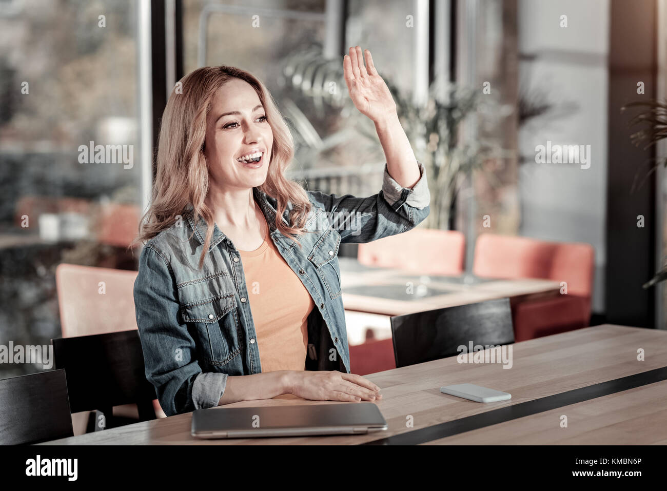 Emotional young woman waving to her friend in a cafe Stock Photo - Alamy