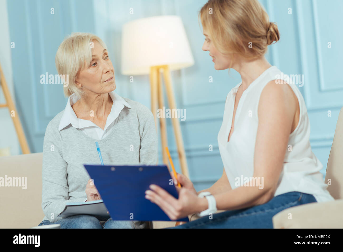 Cheerful smart financial advisor smiling while helping an aged woman ...