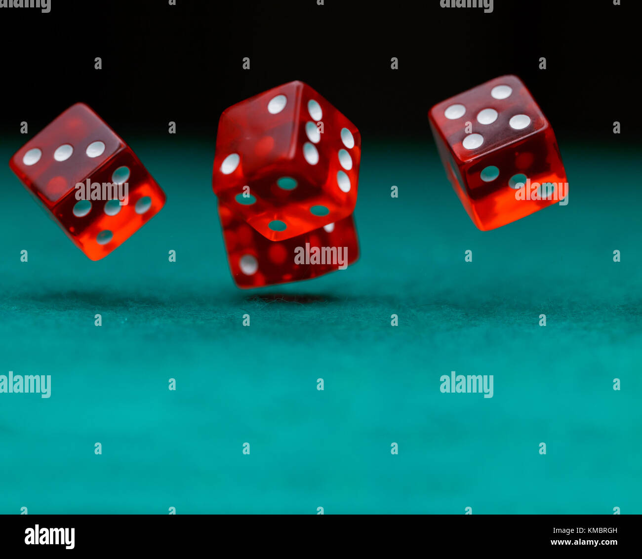 Photo of several red dice falling on green table on black background ...