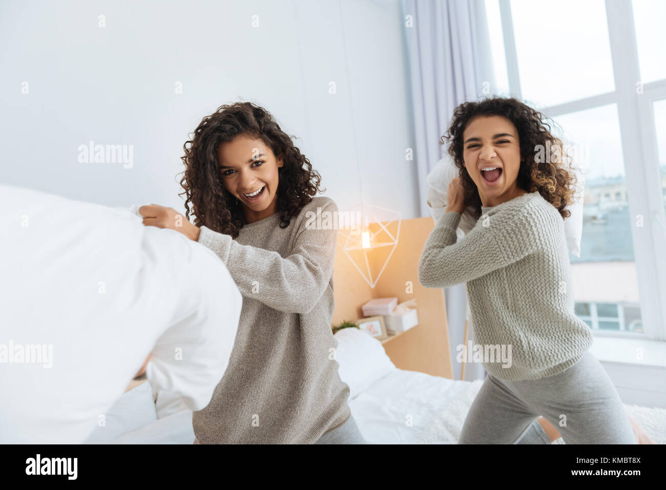 Excited young ladies smiling while fighting with pillows Stock Photo ...