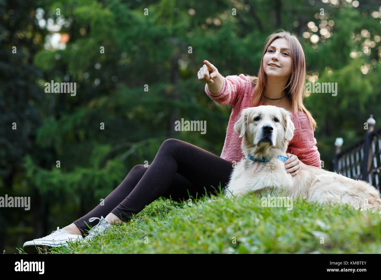 Photo from below of woman pointing forward next to dog on green lawn ...