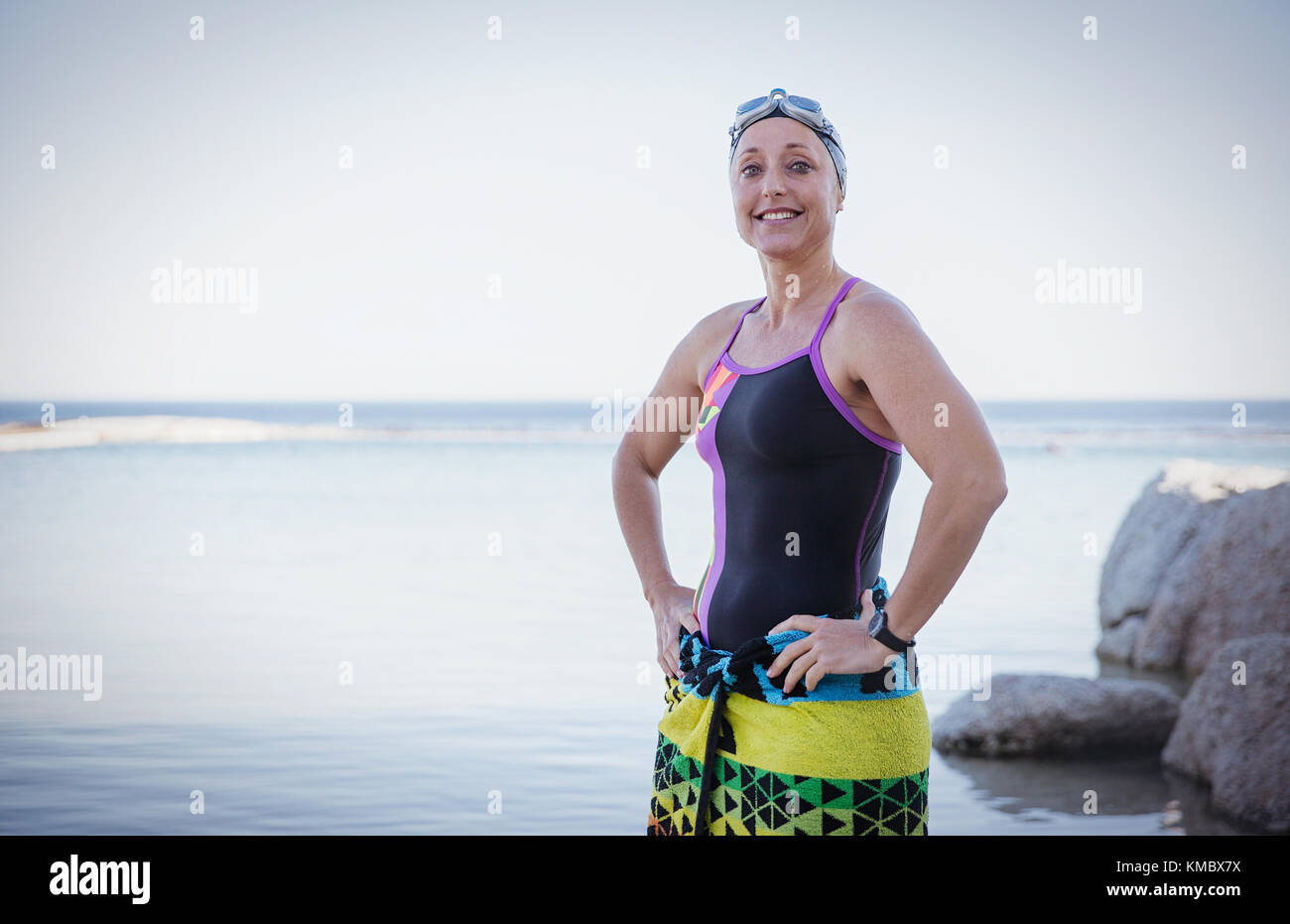 Portrait smiling, confident open water swimmer wrapped in a towel in ...