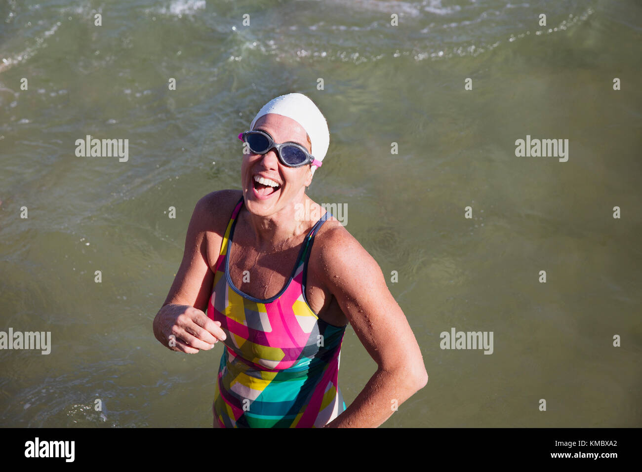 Portrait laughing, confident female open water swimmer wading in ocean ...