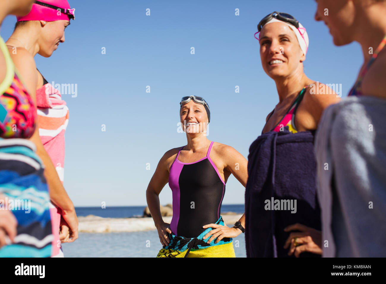 Smiling female open water swimmers wrapped din towels on sunny beach ...