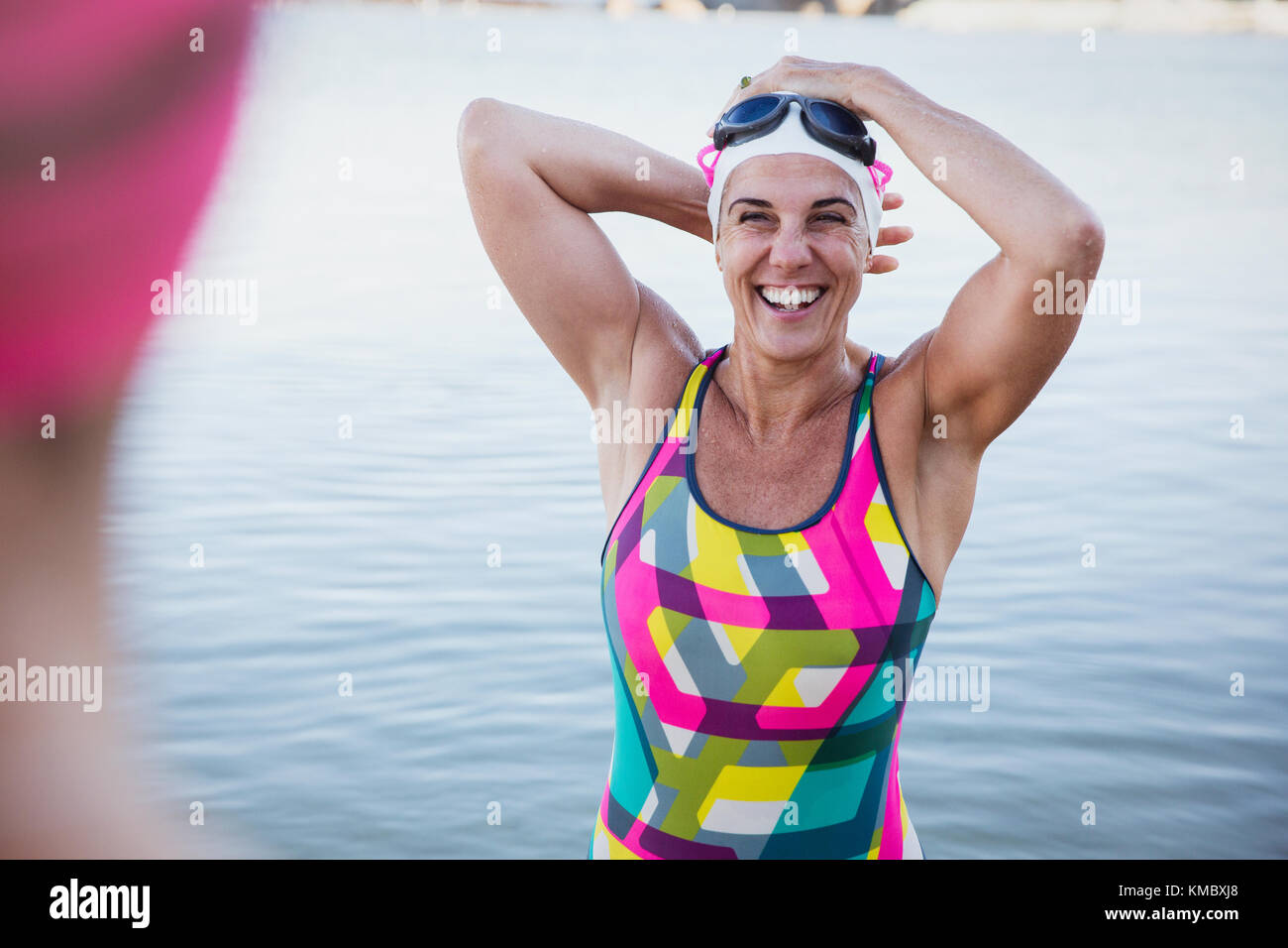 Portrait laughing, smiling female open water swimmer adjusting swimming ...