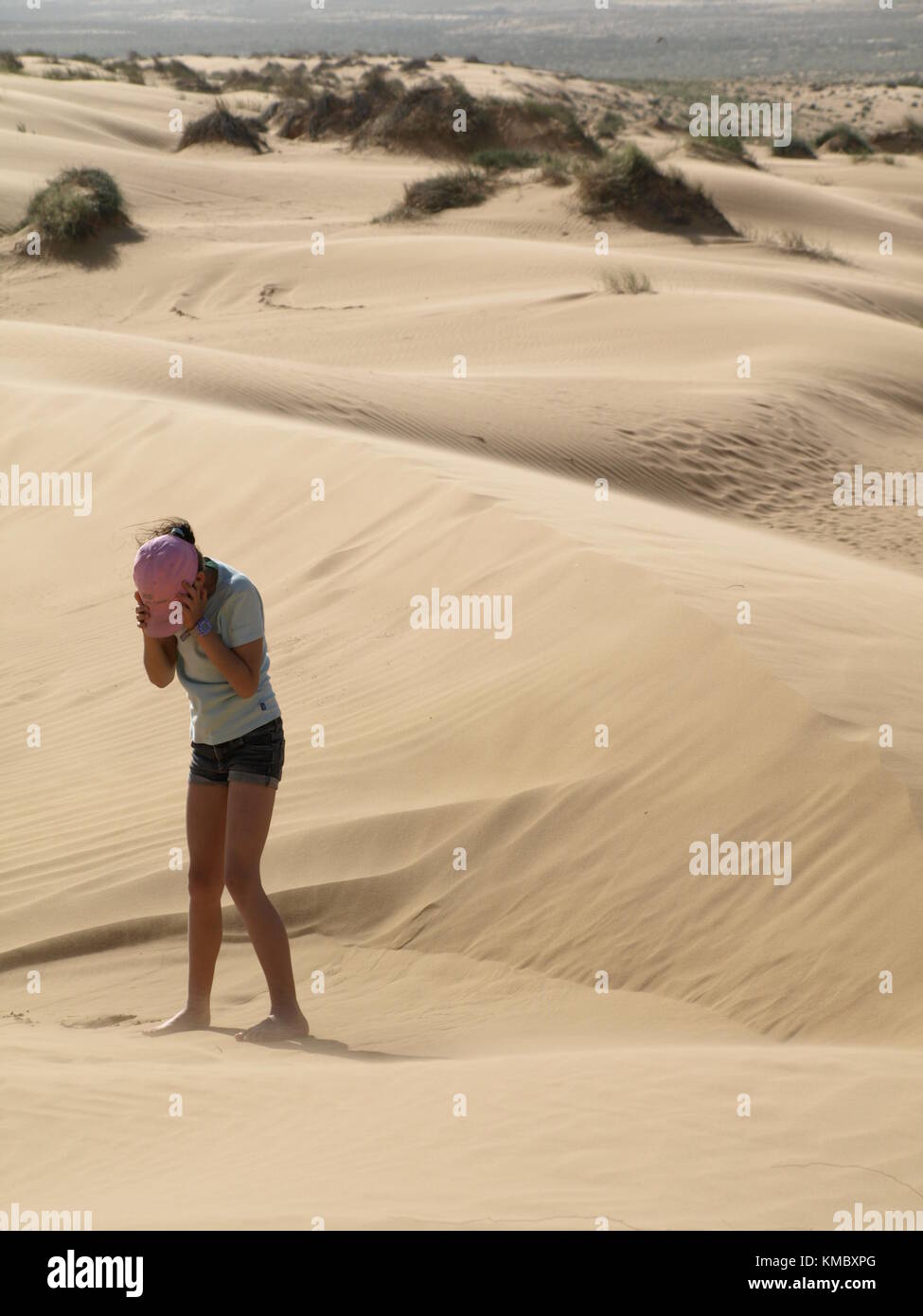 girl standing on sand dune and covering her face from sand storm in the ...